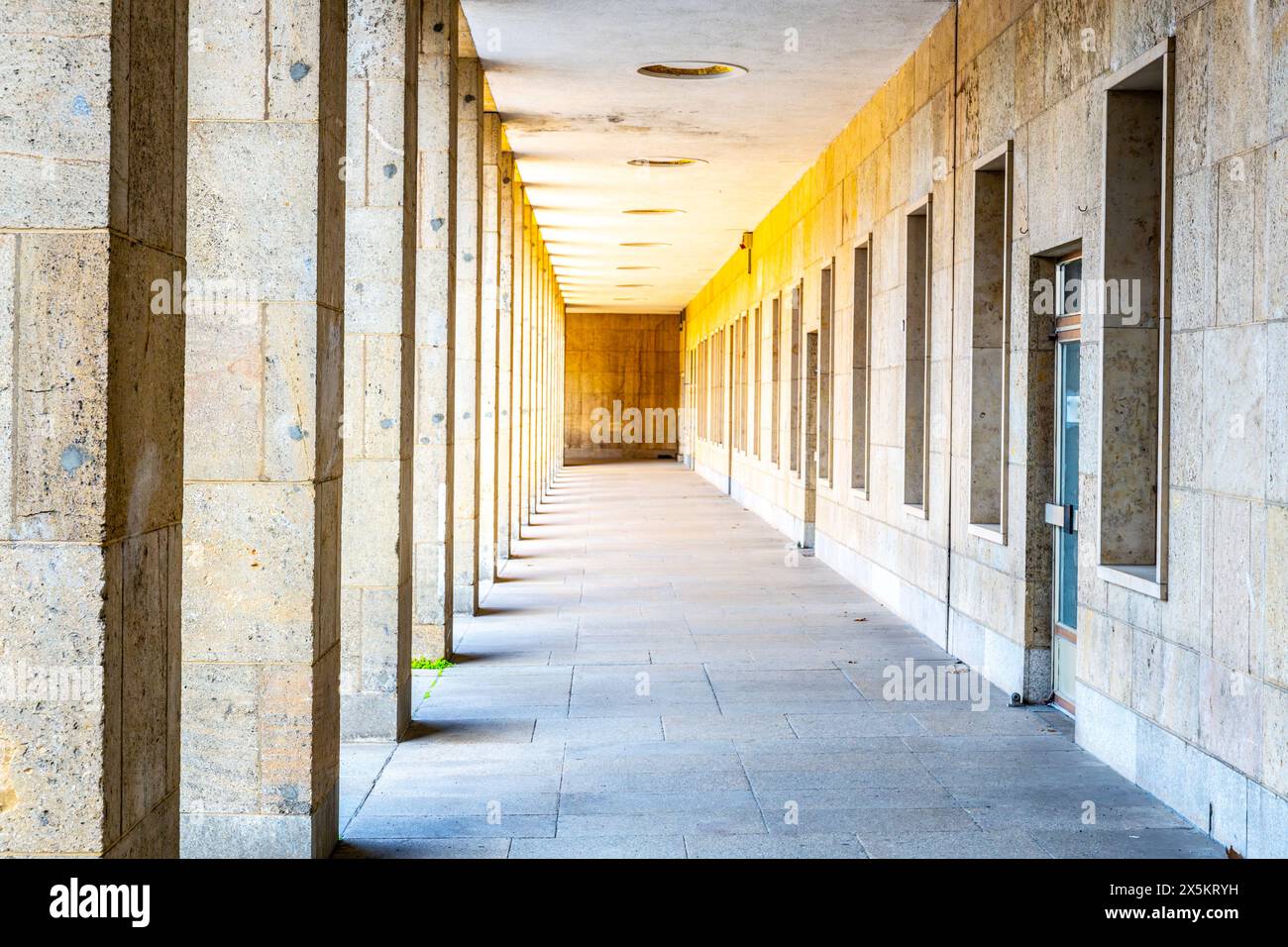 A corridor lined with columns and doors is bathed in sunlight, creating ...