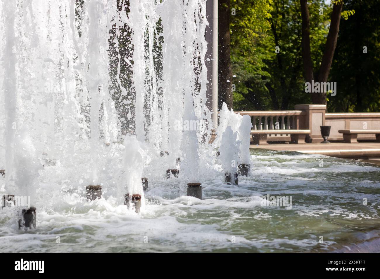 A fountain in a park with trees in the background, the flowing water ...