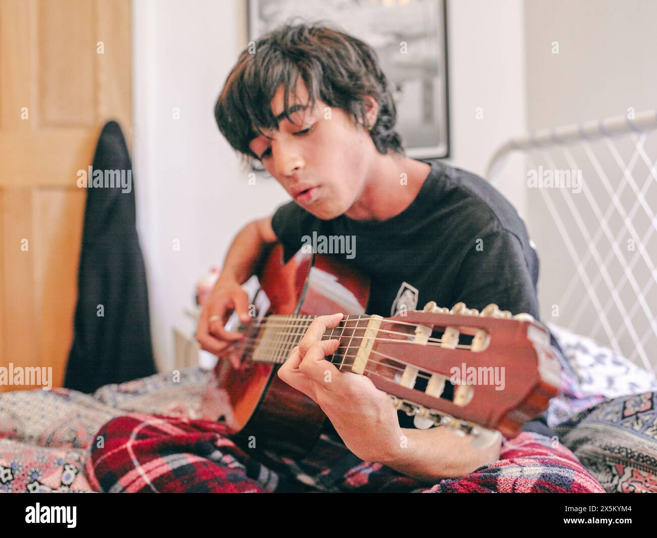 Teenage boy playing acoustic guitar on bed Stock Photo - Alamy