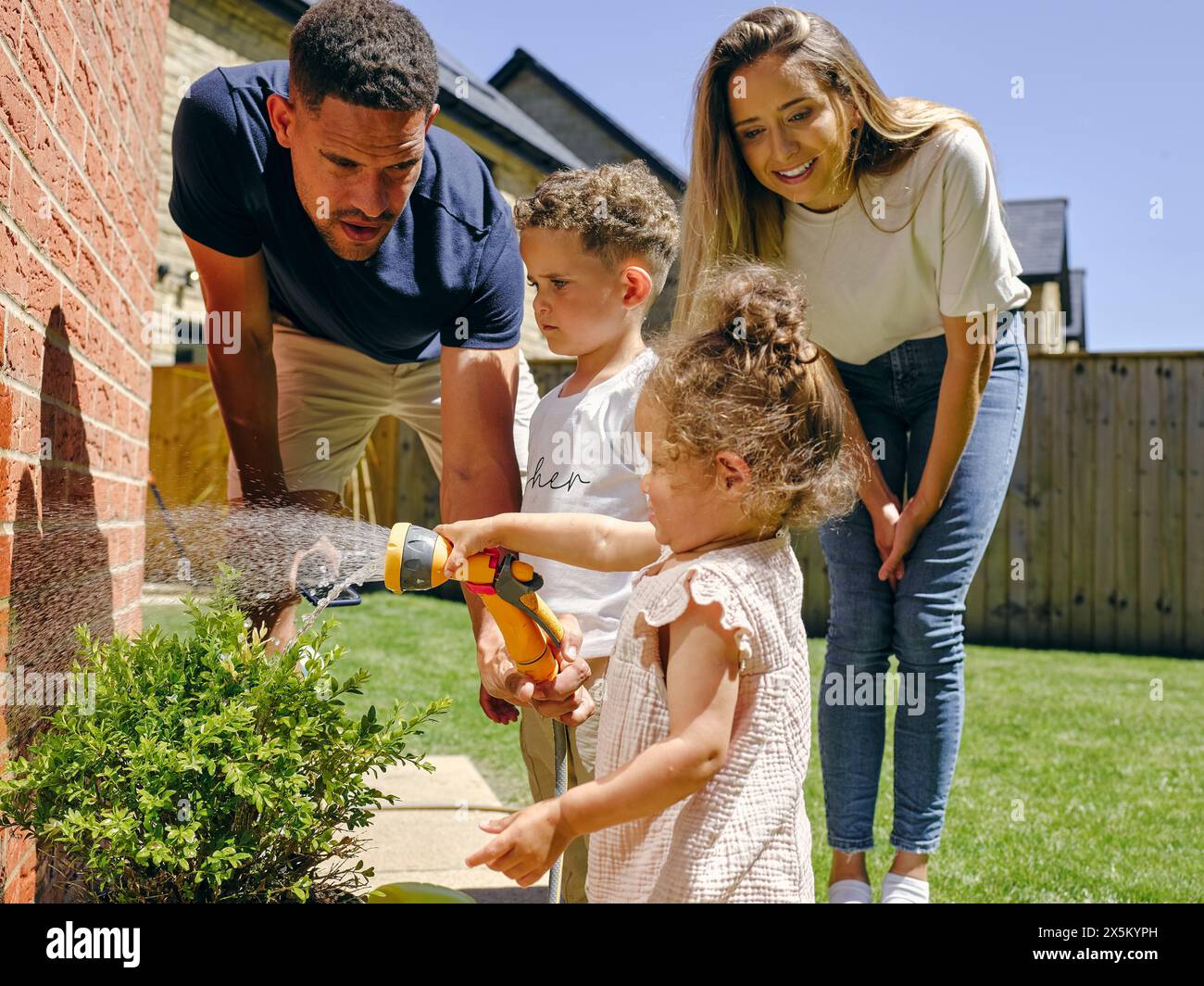 Parents with children watering plant in back yard Stock Photo - Alamy