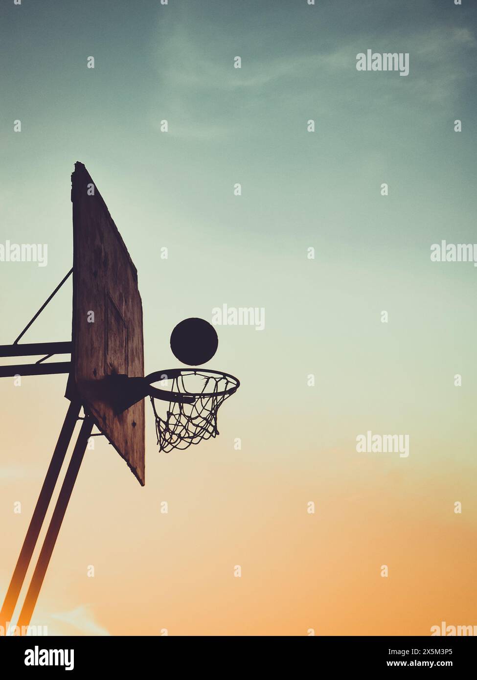 Basketball falling into basketball hoop against sky at sunset Stock ...