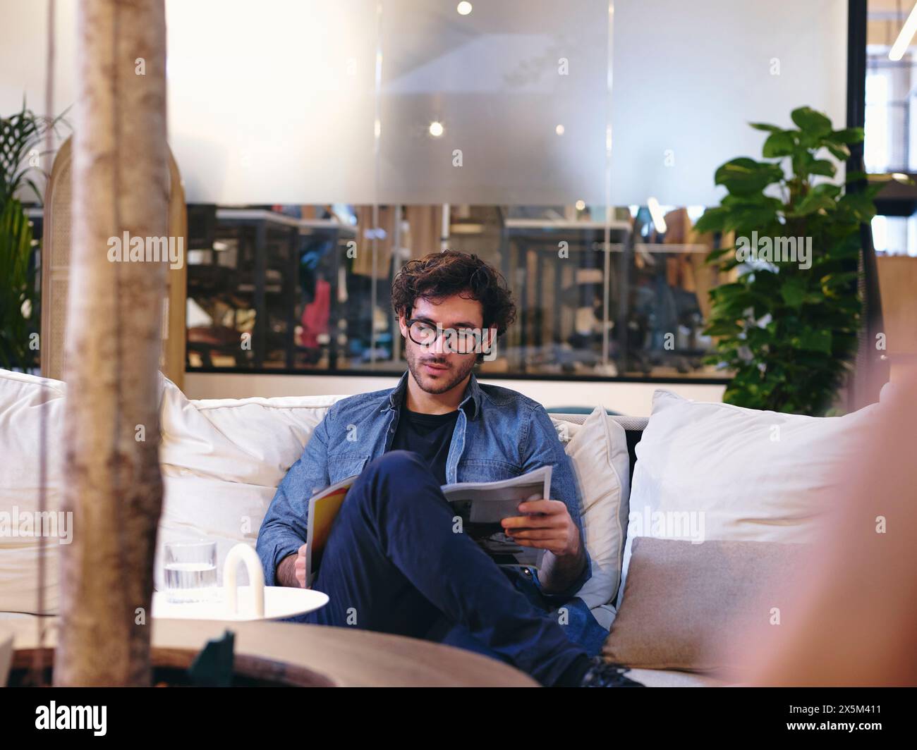 UK, London, Man reading magazine on sofa in modern office lobby Stock ...