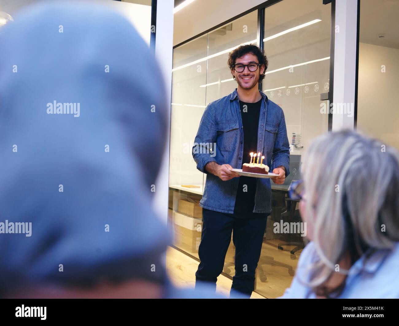UK, London, Smiling man with birthday cake entering conference room ...