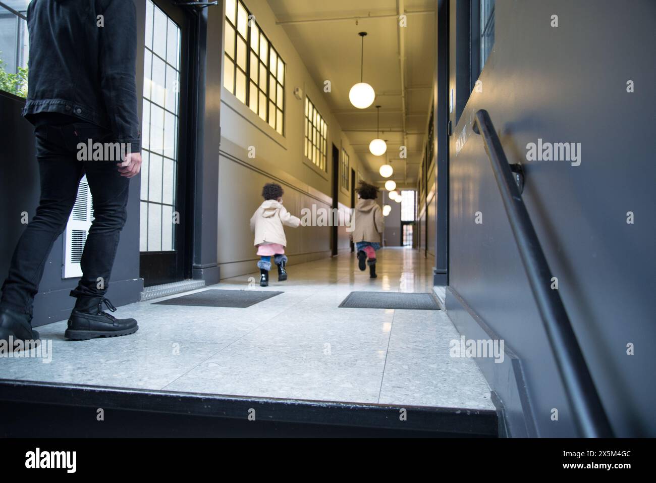 Father following daughters running down corridor Stock Photo - Alamy