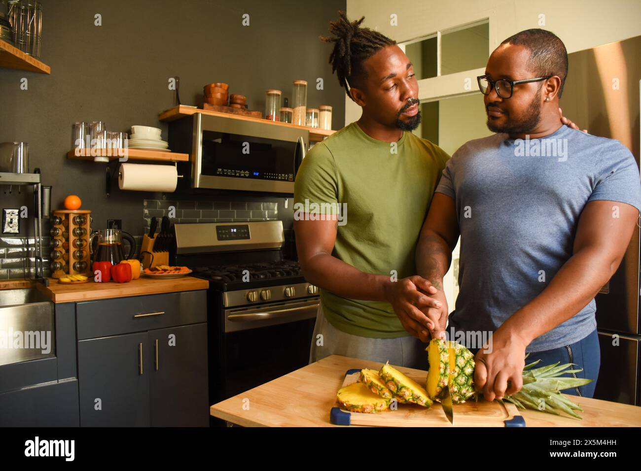 Male couple cutting pineapple in kitchen Stock Photo - Alamy