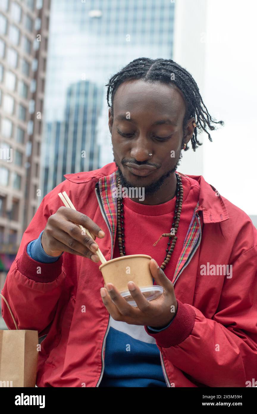 Young man eating Asian take out food in city Stock Photo - Alamy