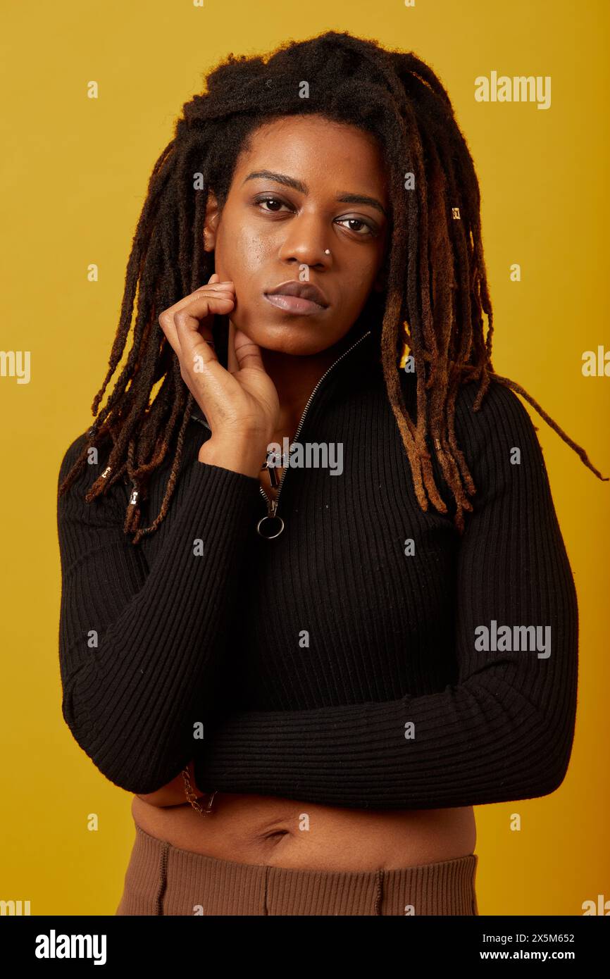 Studio portrait of woman with dreadlocks against yellow background ...