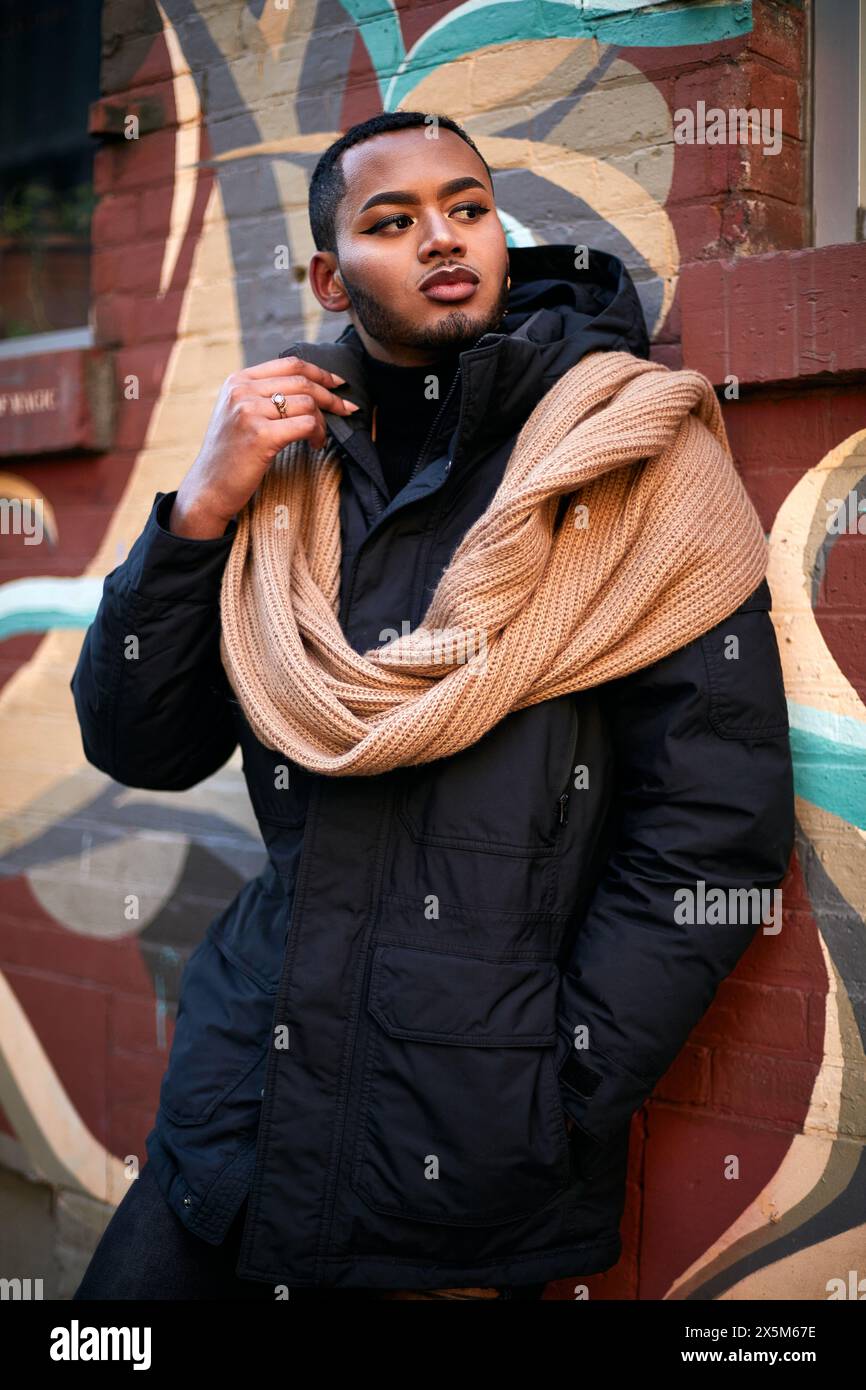 USA, New York City, Queer man in jacket and scarf against wall with ...