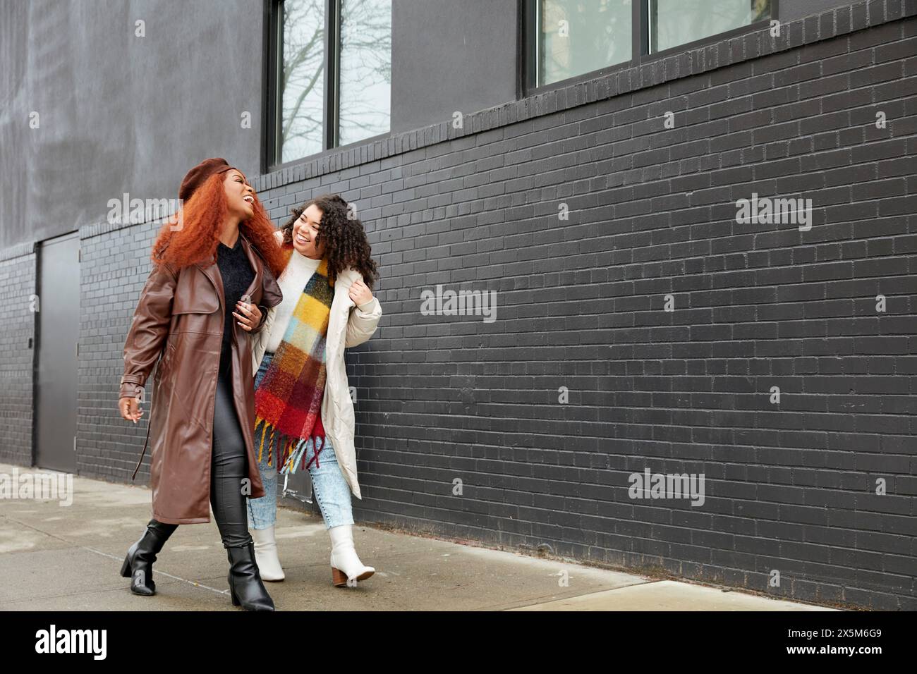 Smiling women walking alongside black building Stock Photo - Alamy