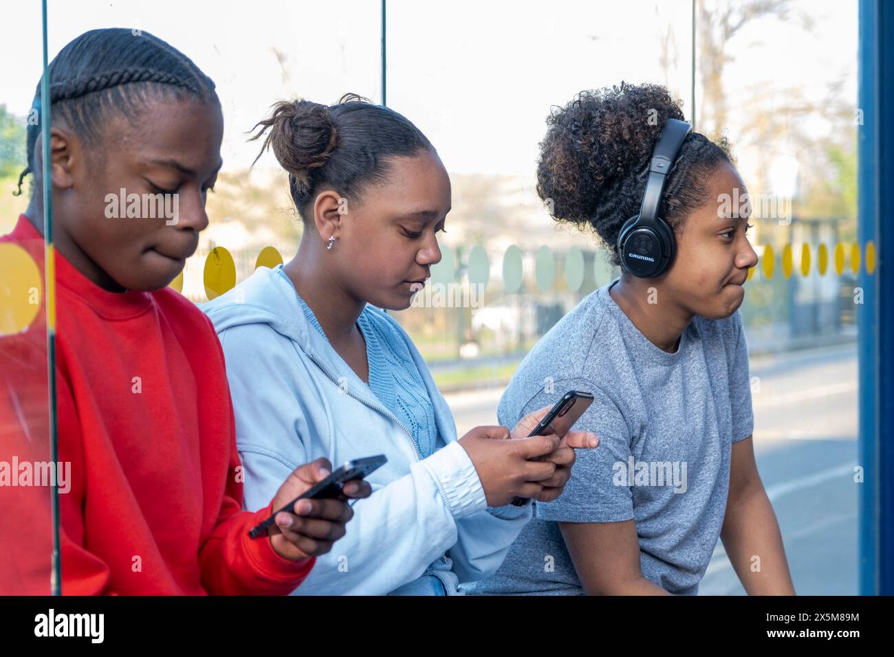 Friends sitting at bus stop and using phones Stock Photo - Alamy