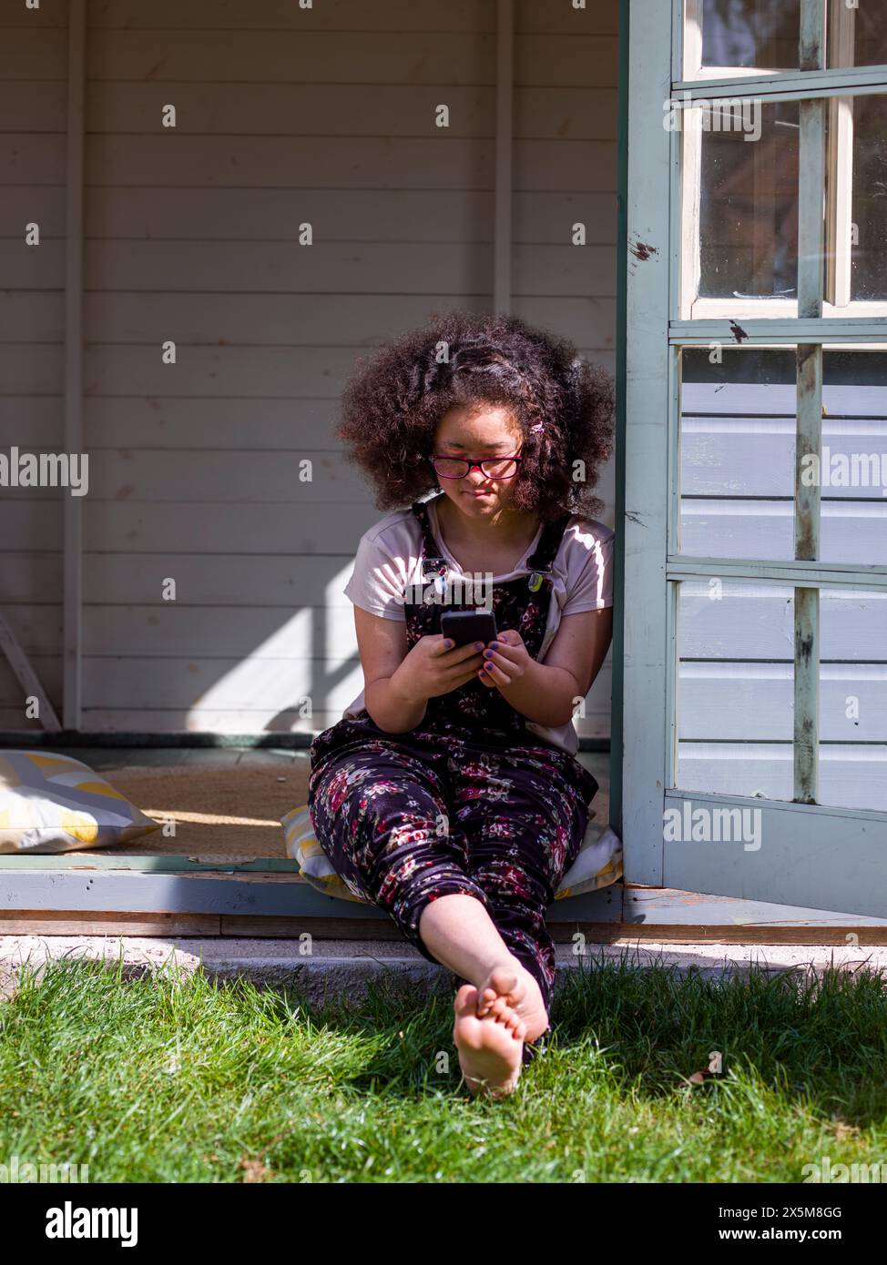 Girl with smartphone sitting on porch Stock Photo - Alamy