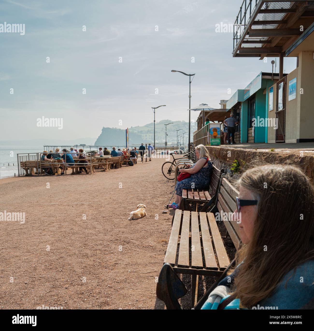 Two woman seated on public seating in the sun on Teignmouth sea front ...