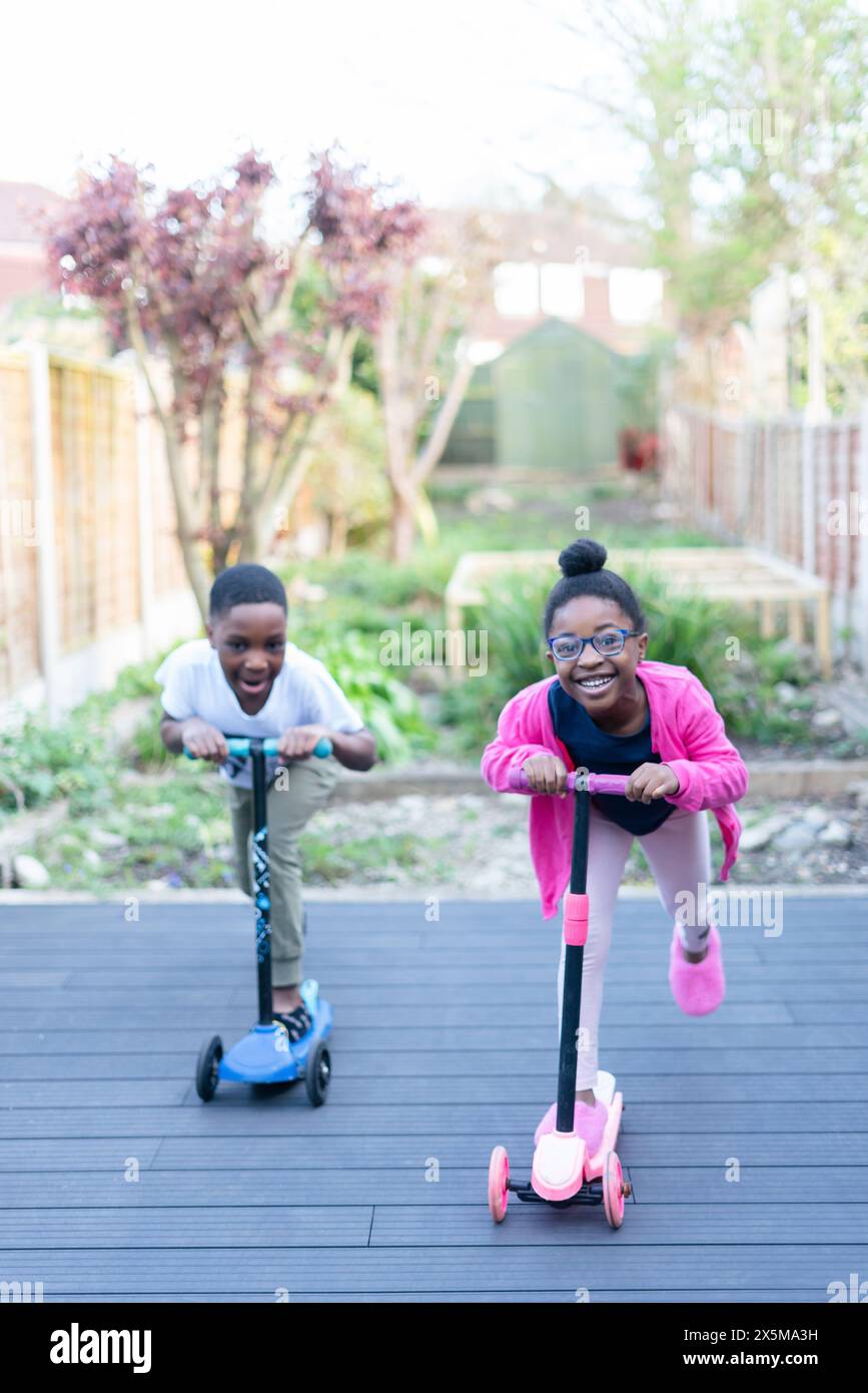 Siblings on push scooters in backyard Stock Photo - Alamy
