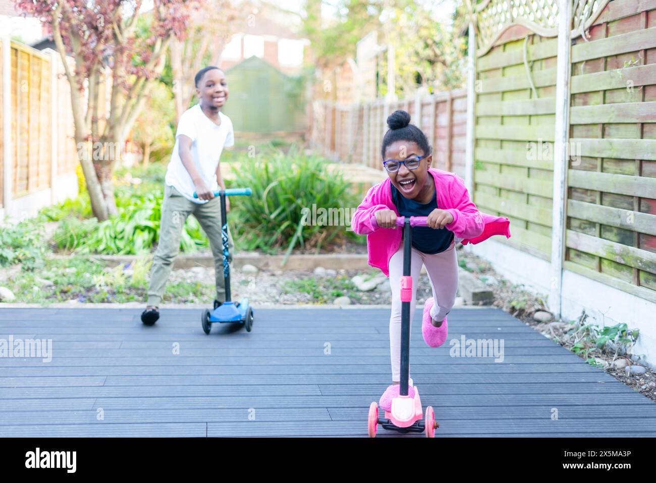Siblings on push scooters in backyard Stock Photo - Alamy