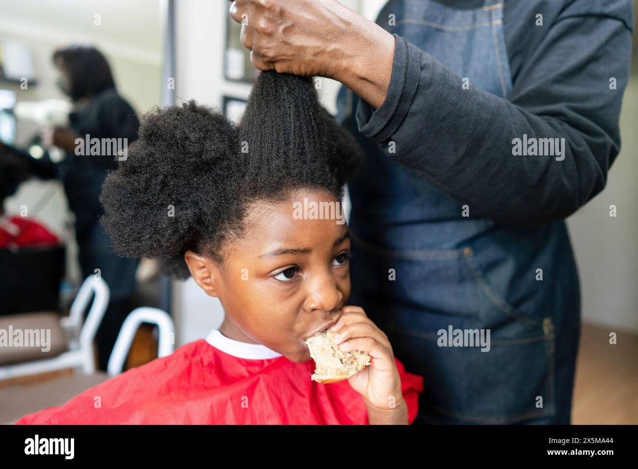 Girl eating while having hair done by hairdresser Stock Photo - Alamy