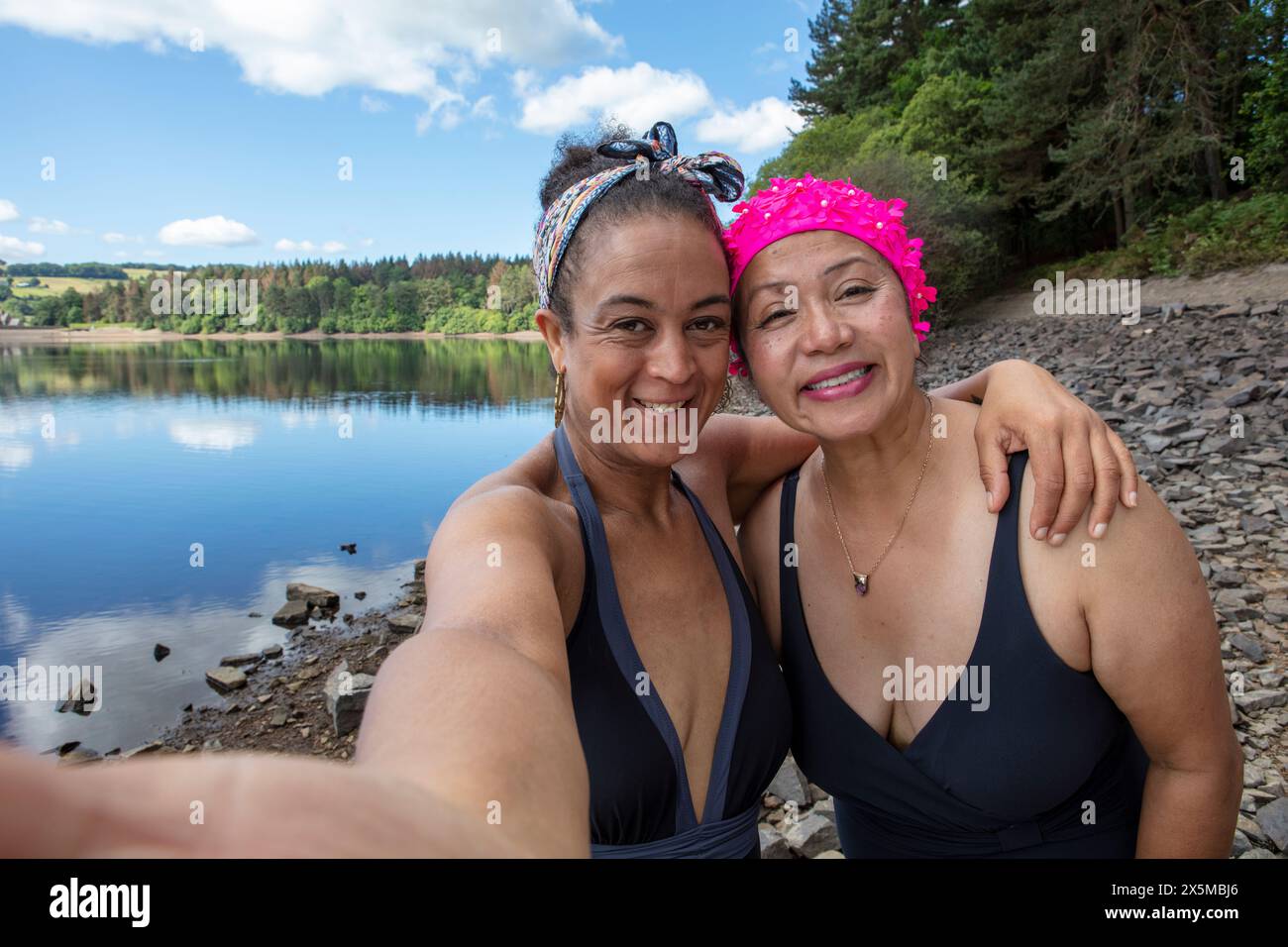 Portrait of smiling women in swimsuits on rocky lakeshore, Yorkshire ...