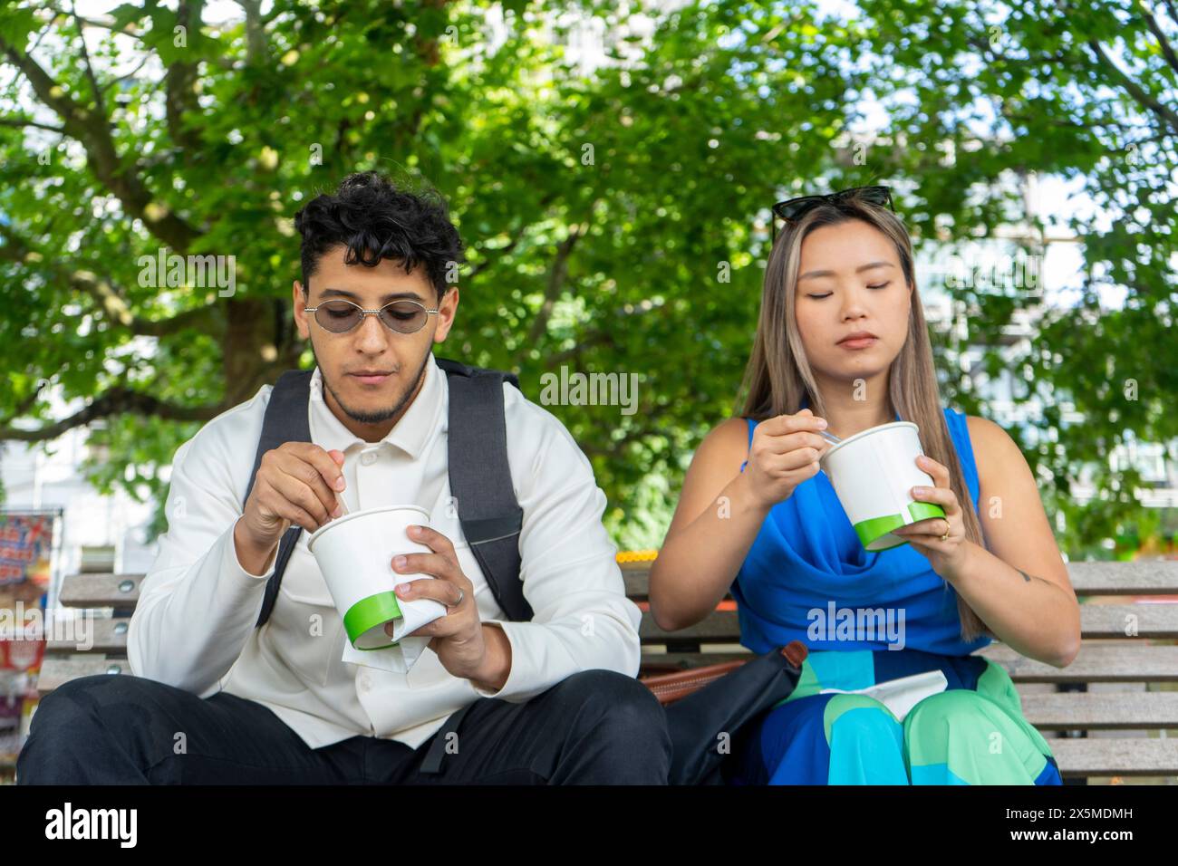 Tourist couple sitting on park bench eating street food Stock Photo - Alamy