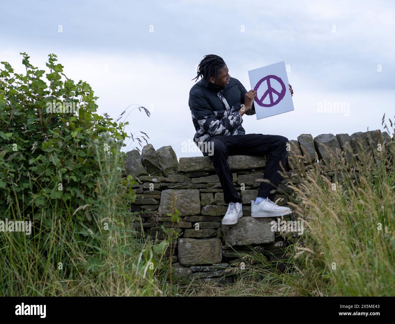 Young man sitting on stone wall holding peace sign Stock Photo - Alamy