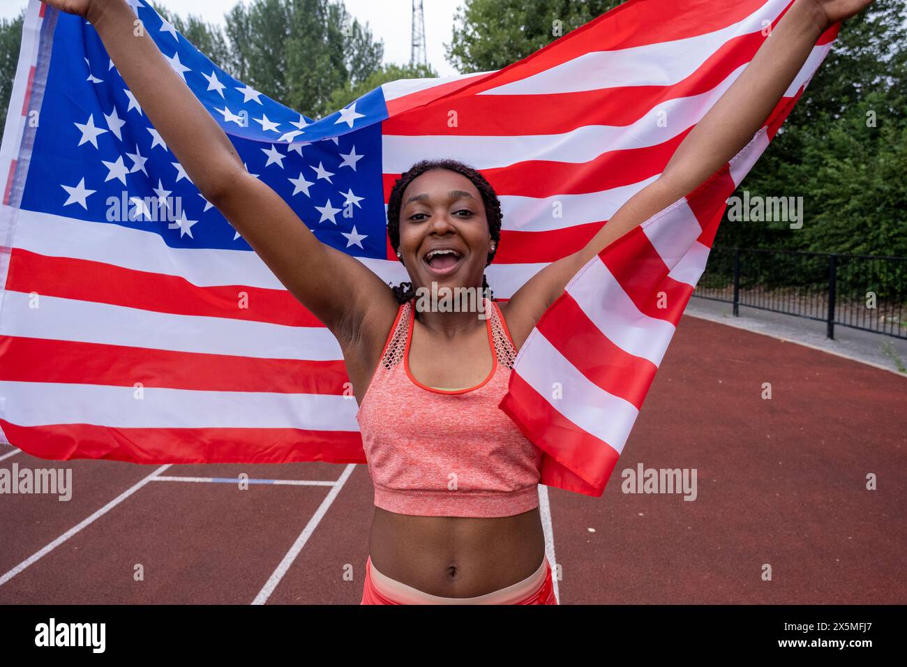 Portrait of smiling athletic woman with American flag on running track ...