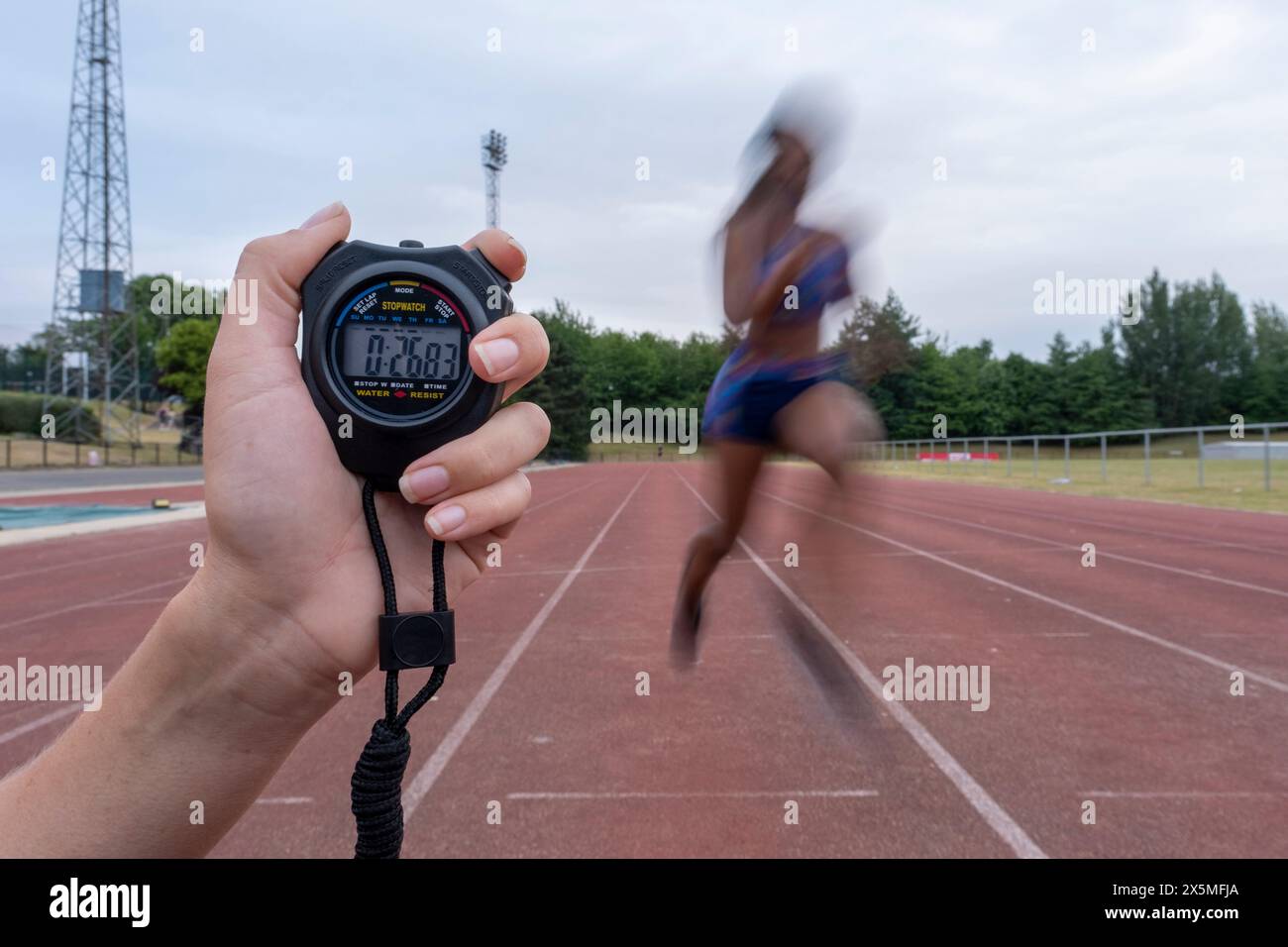 Athletic woman running on track, hand holding stopwatch in foreground ...