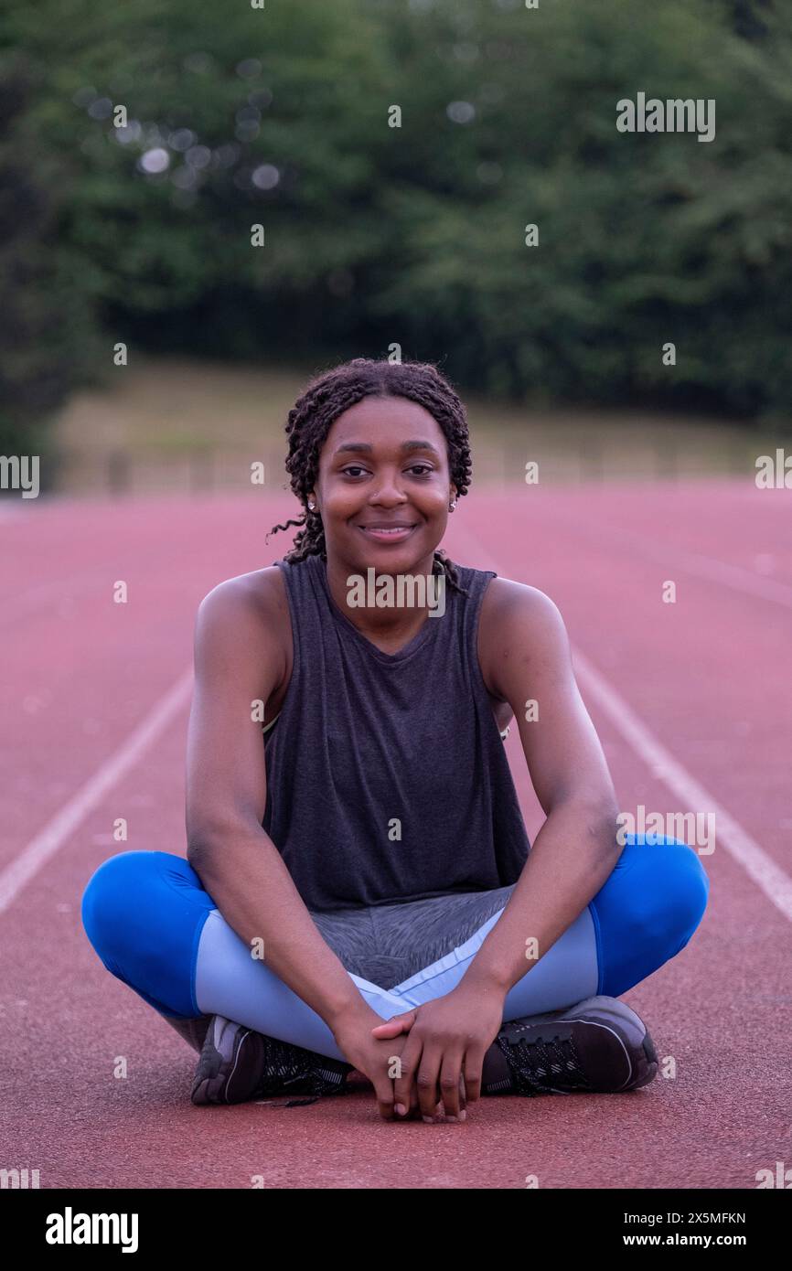 Portrait of smiling athletic woman sitting on running track Stock Photo ...