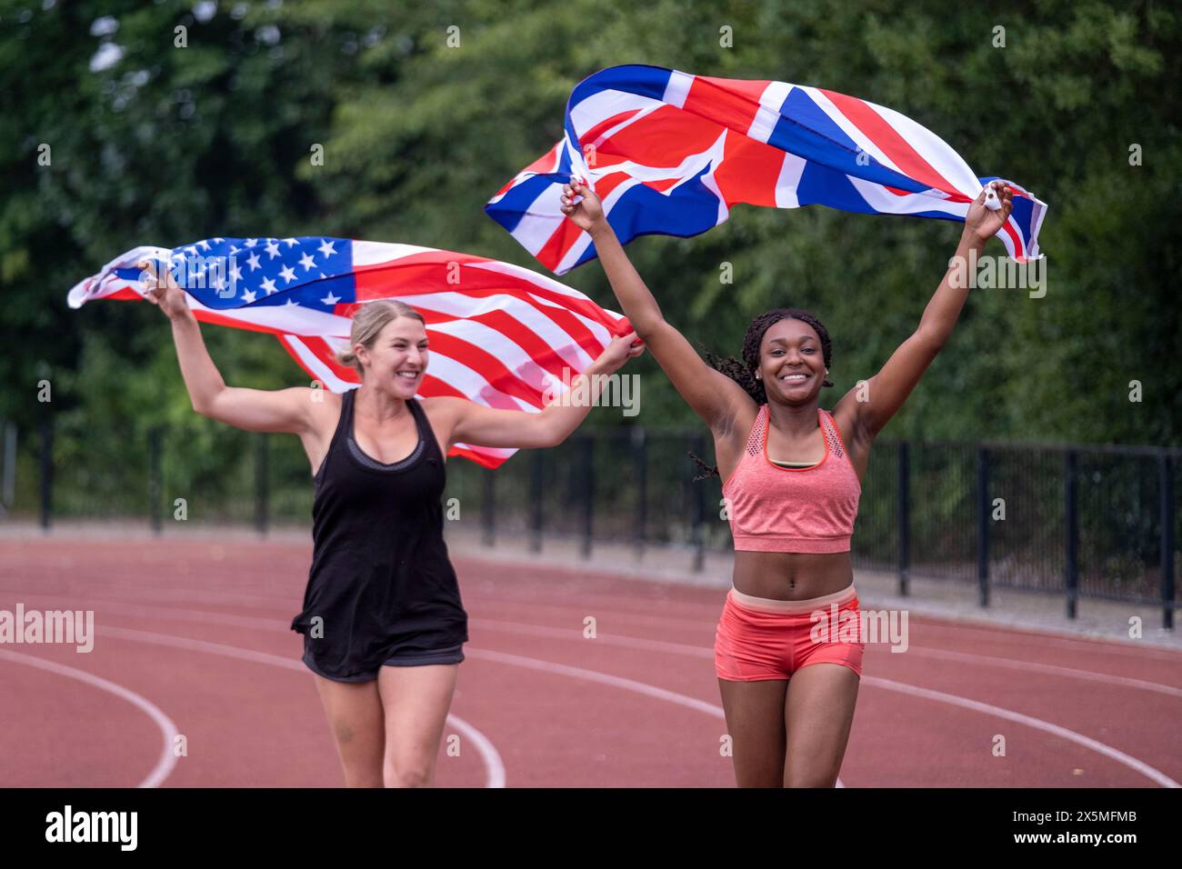 Two female athletes running with flags on running track Stock Photo - Alamy