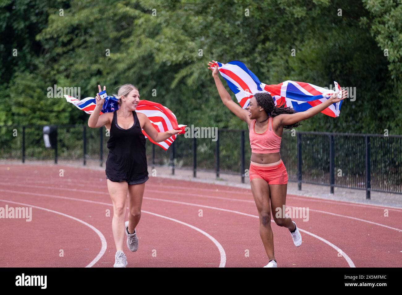 Two female athletes running with flags on running track Stock Photo - Alamy