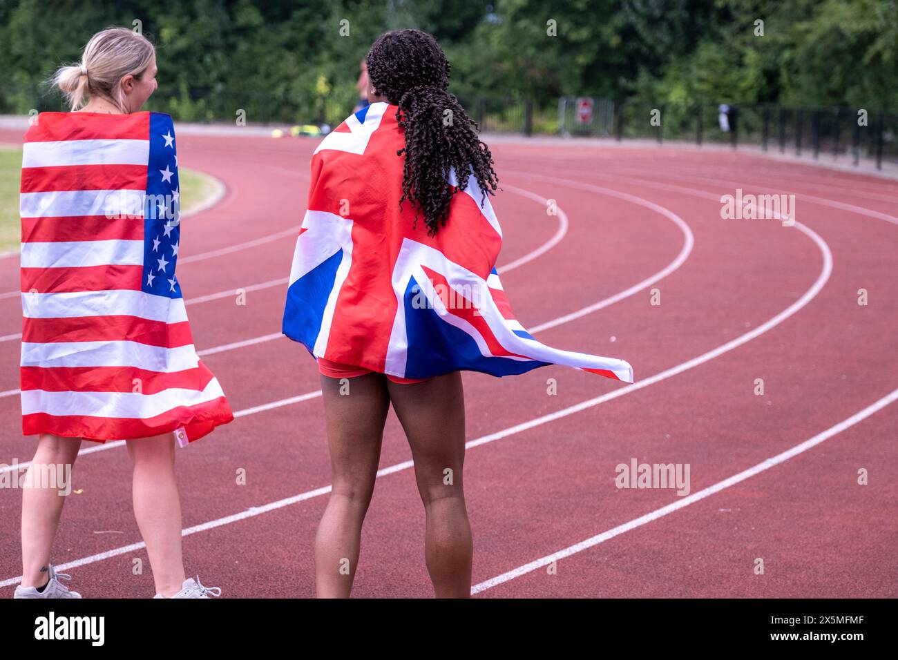 Rear view of two female runners wrapped in flags on running track Stock ...