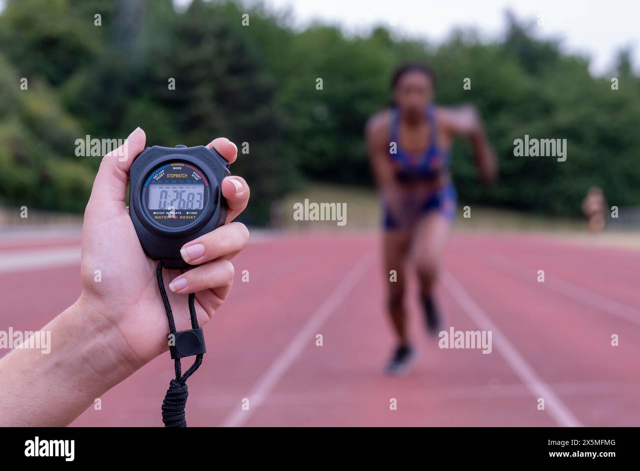 Female athlete running on running track, hand with stopwatch in ...