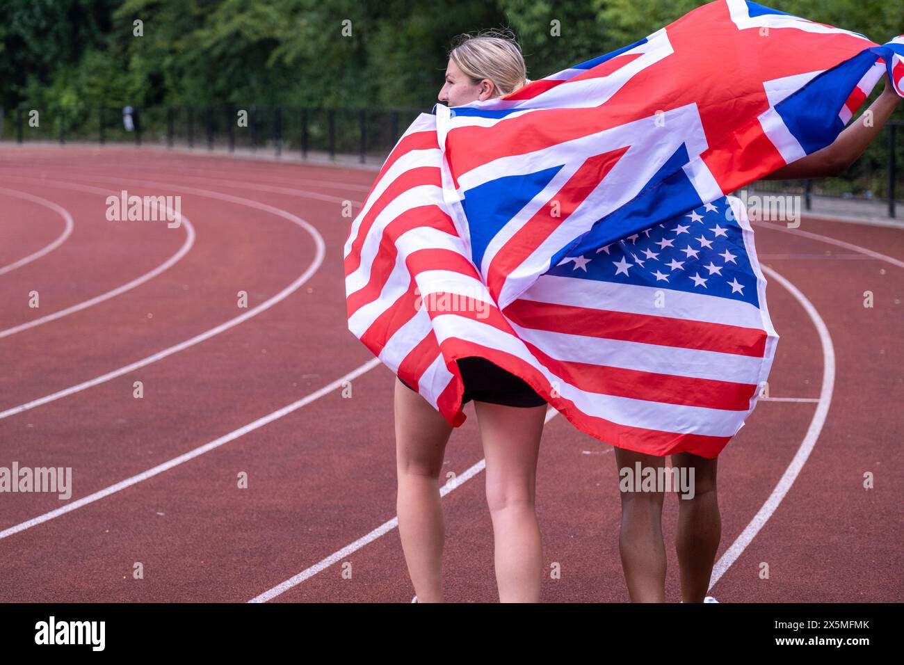 Rear view of two female runners wrapped in flags on running track Stock ...