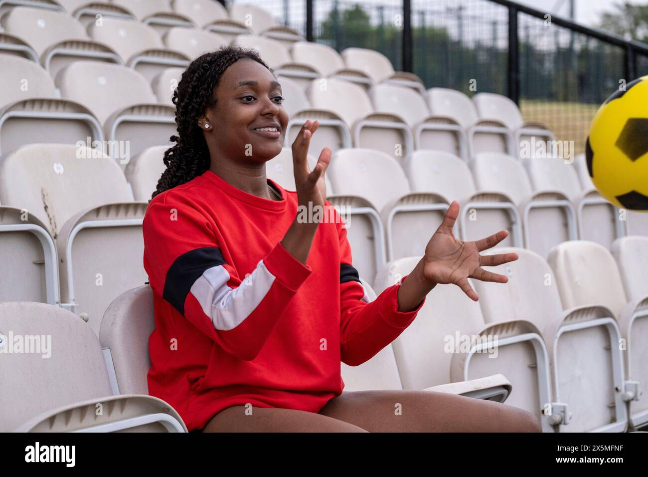 Smiling athletic woman sitting on chair at stadium, catching soccer ...