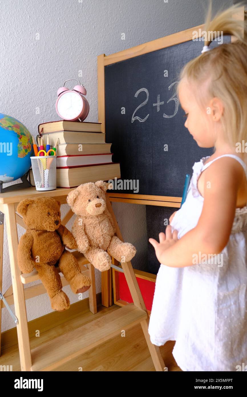 child, blonde girl plays school, small teacher teaches lesson, student ...