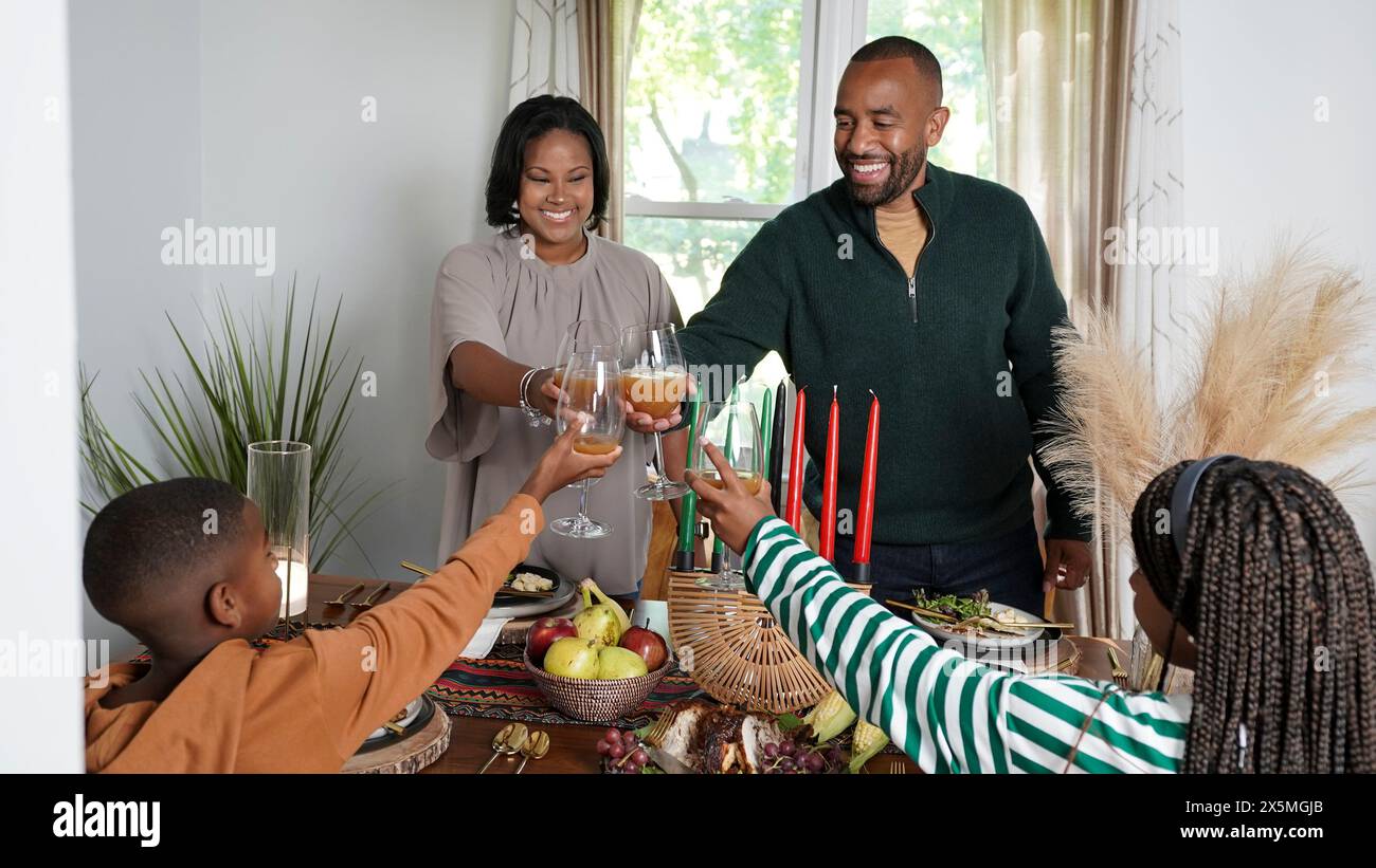 Family with children (8-9, 12-13) raising toast during Kwanzaa meal ...