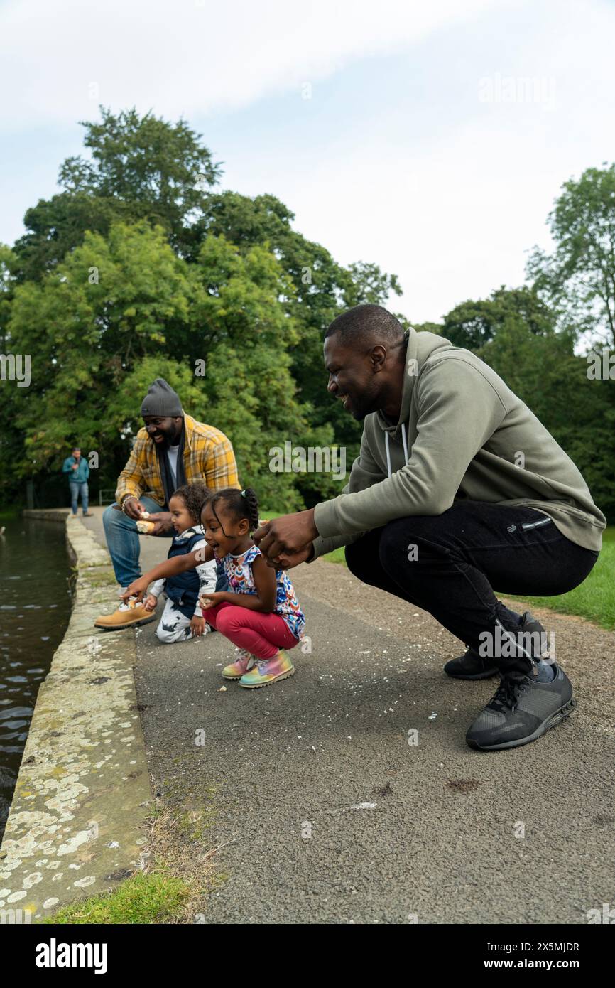 Two men with daughters crouching by pond in park Stock Photo - Alamy