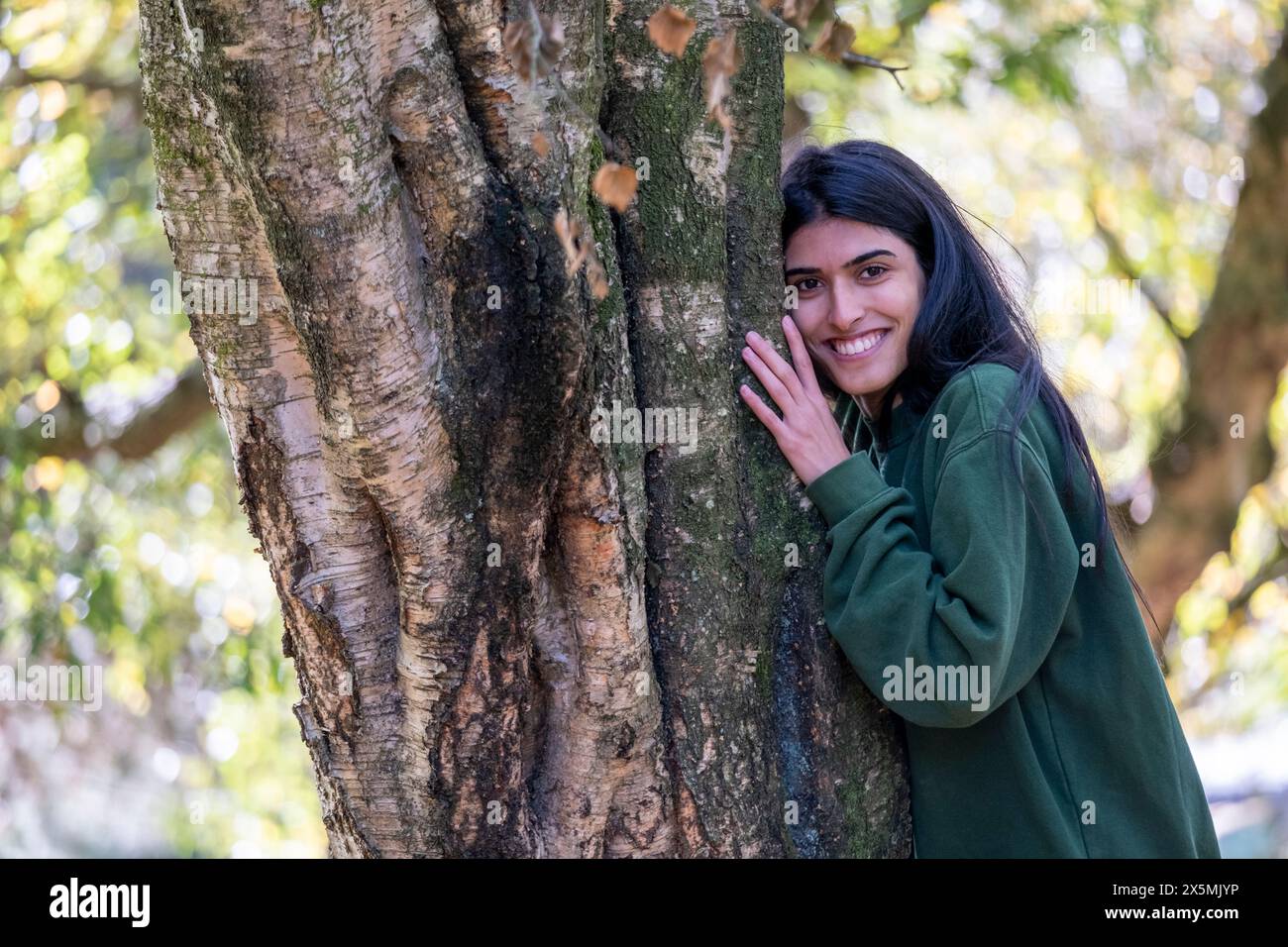 Portrait of smiling woman touching tree in forest Stock Photo - Alamy