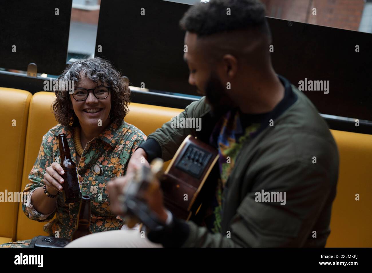 Young man playing acoustic guitar in office lounge, woman drinking ...