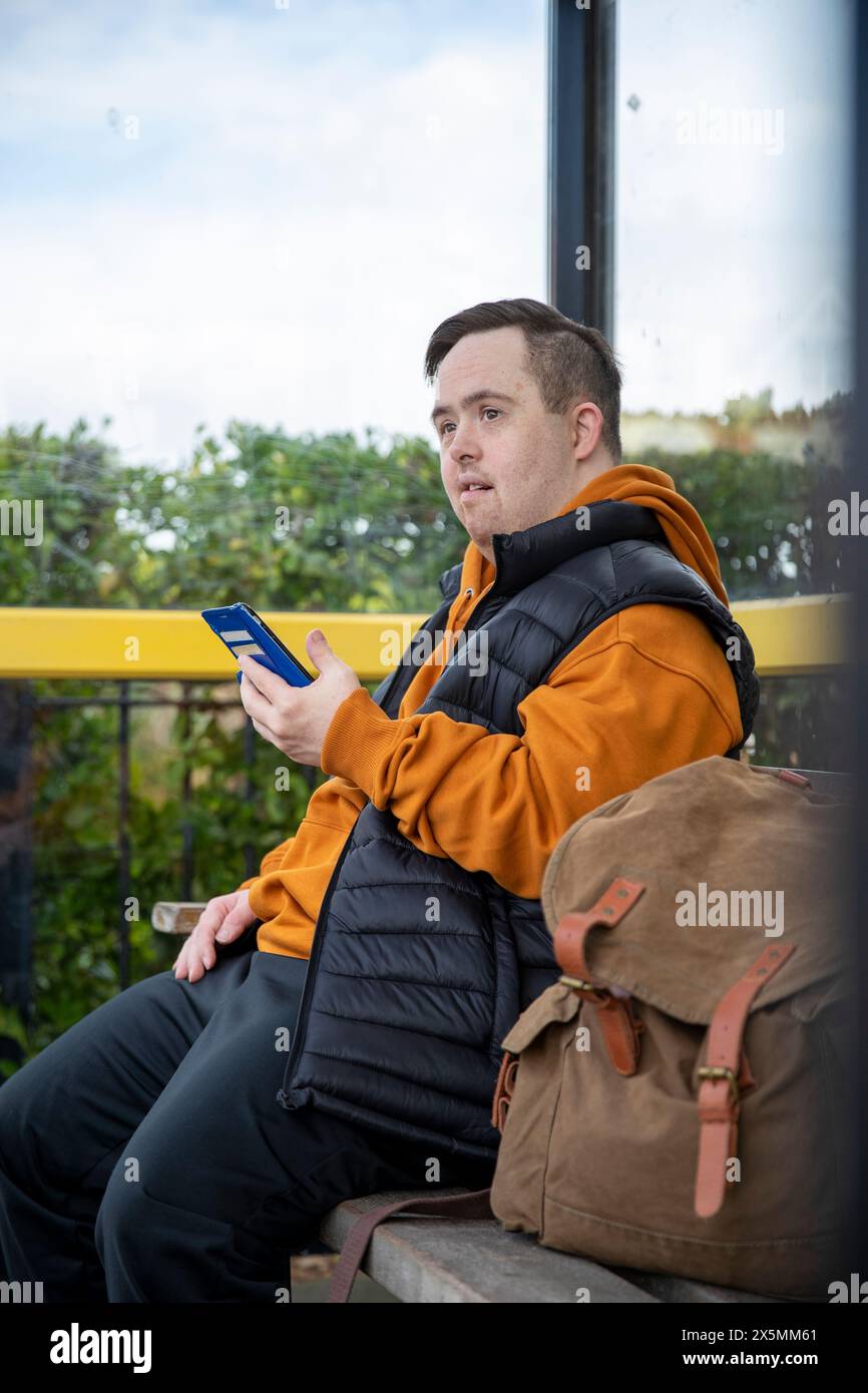 Man sitting on bench at bus stop, using smart phone Stock Photo - Alamy