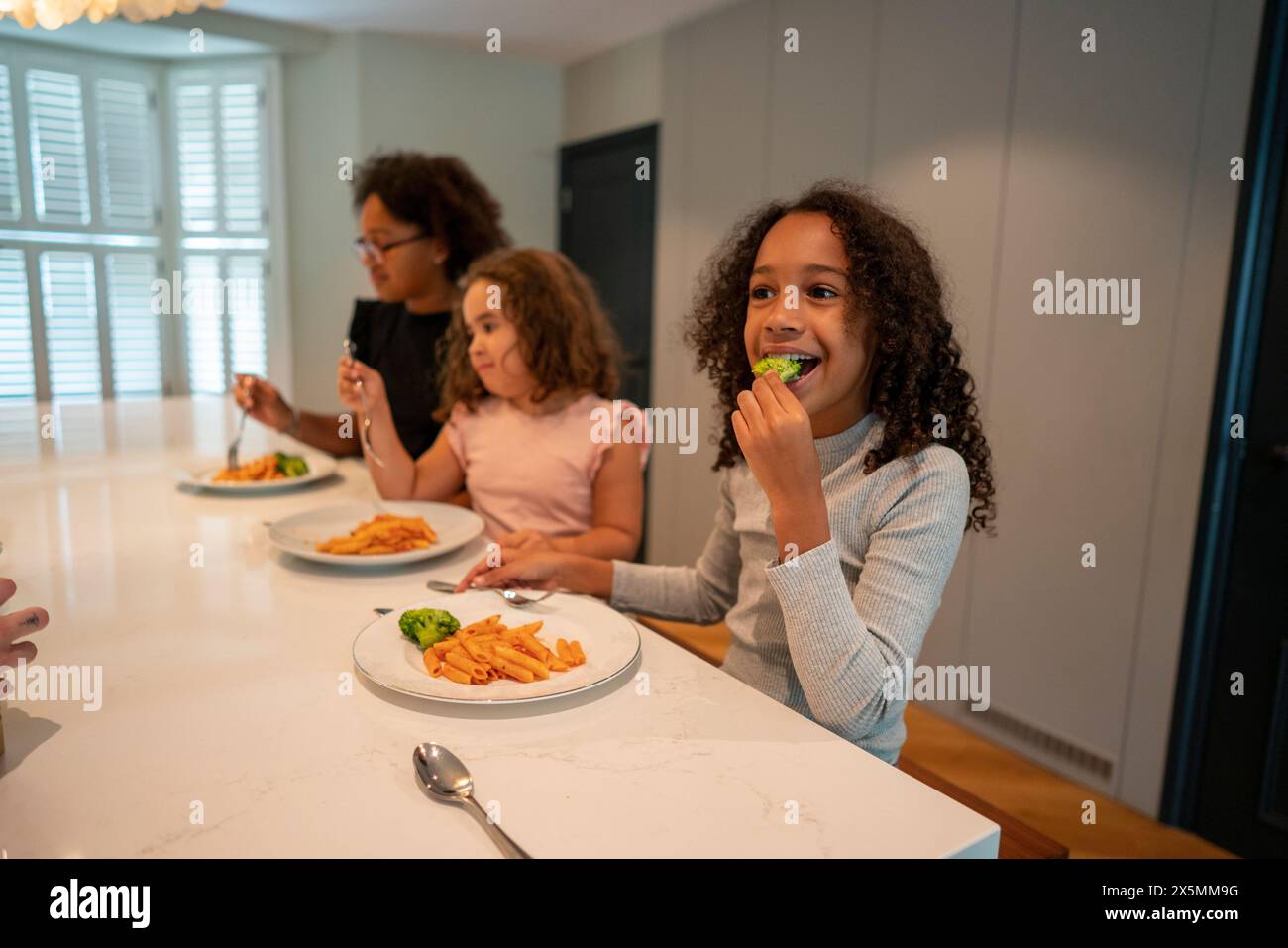 Three smiling sisters enjoying dinner in kitchen Stock Photo - Alamy