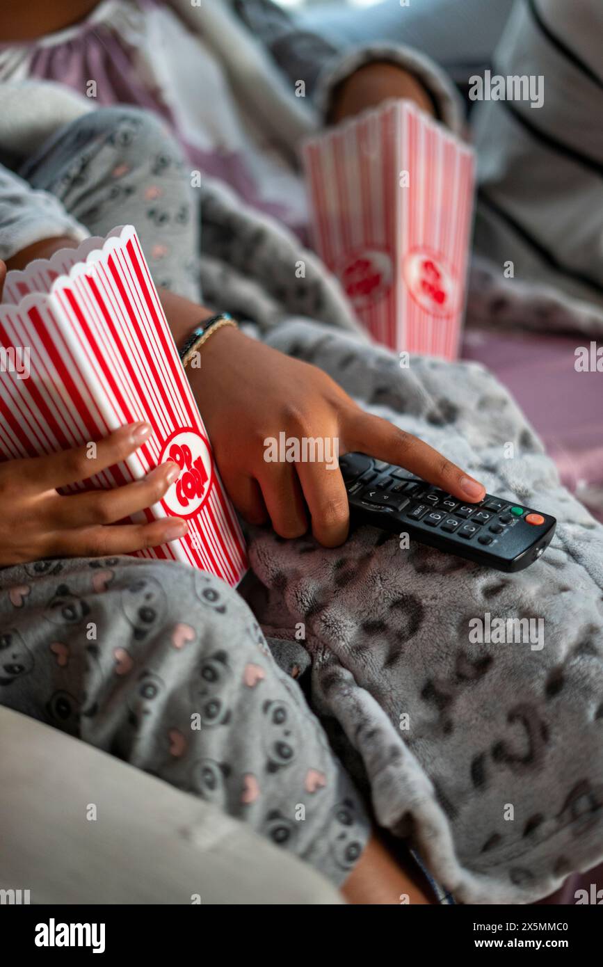Close-up of sisters holding remote control and popcorn Stock Photo - Alamy