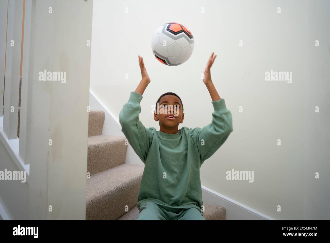 Boy sitting on stairs and throwing soccer ball in air Stock Photo - Alamy