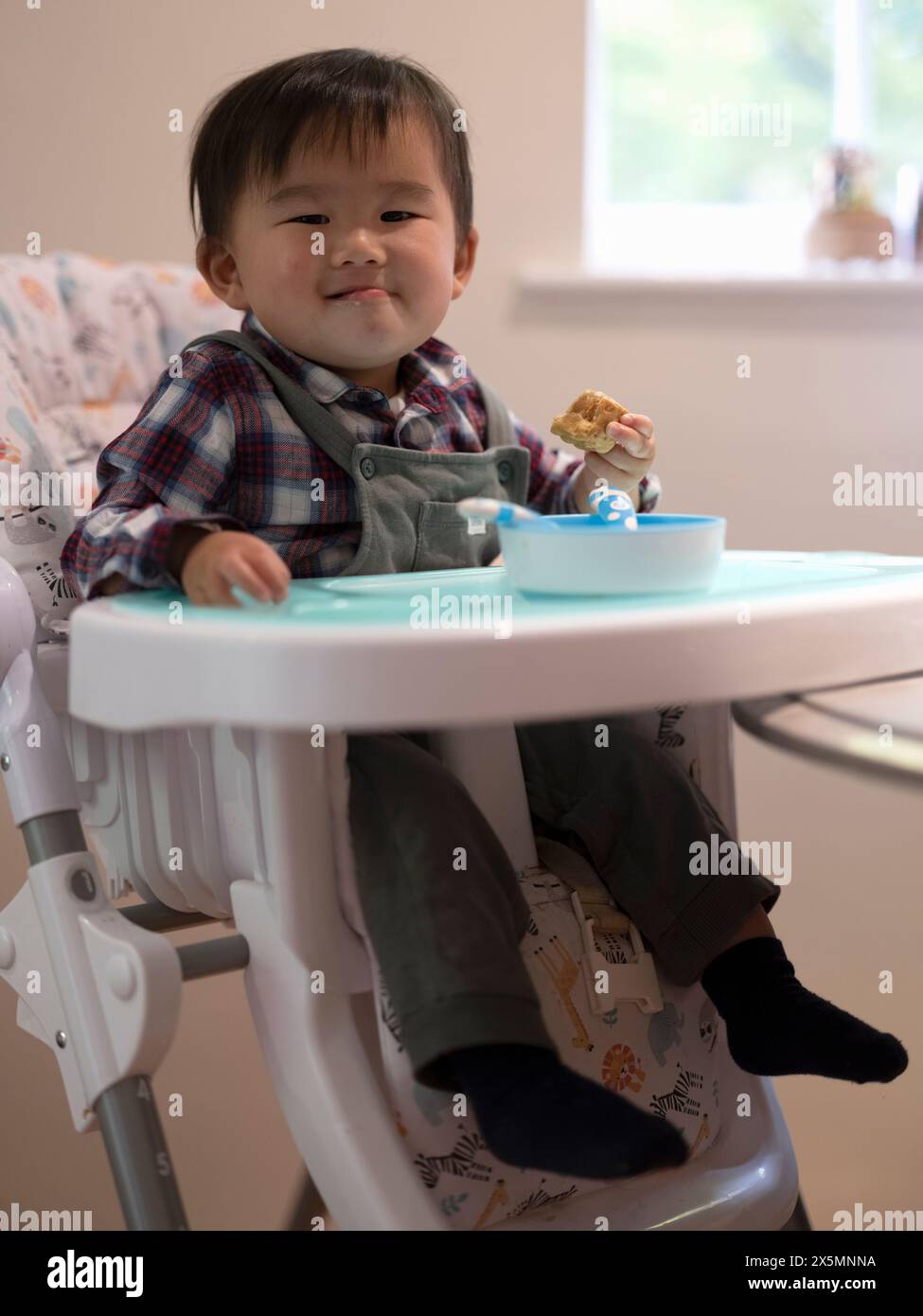 Baby boy sitting in high chair and eating Stock Photo - Alamy