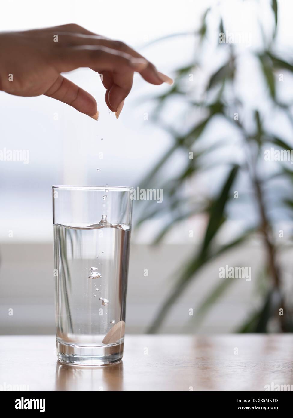 Close-up of womans hand dropping effervescent tablet into glass of ...