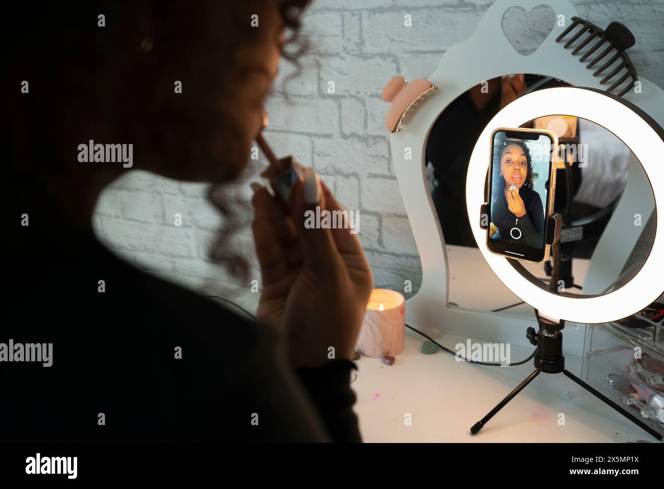 Teenage girl applying lip gloss while filming makeup video at home ...