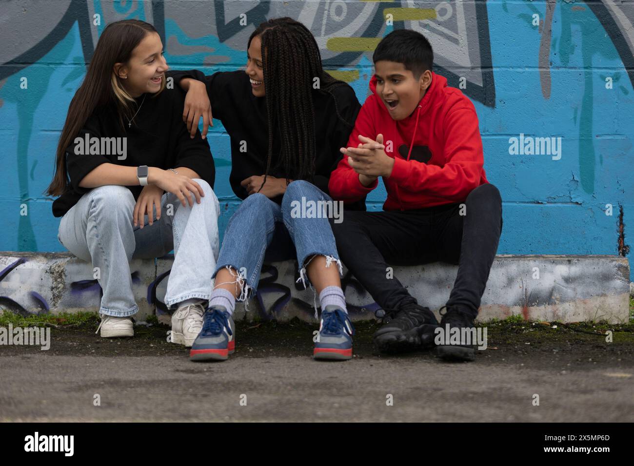 Smiling friends sitting against graffiti wall Stock Photo - Alamy