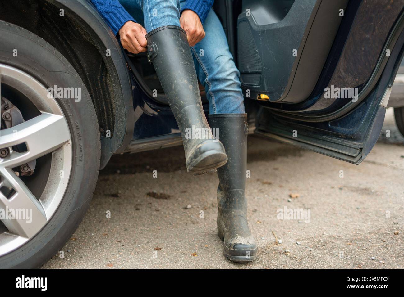 Man sitting on back seat and putting on rubber boot Stock Photo - Alamy