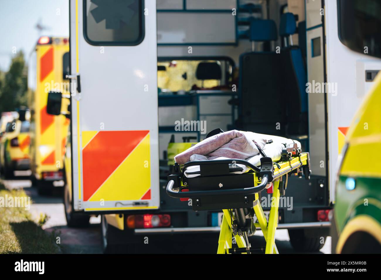 Stretcher prepared behind open ambulance. Teams of emergency medical ...