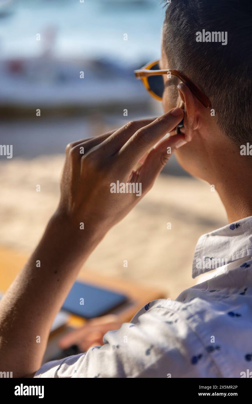 Man on beach adjusting earbuds Stock Photo - Alamy