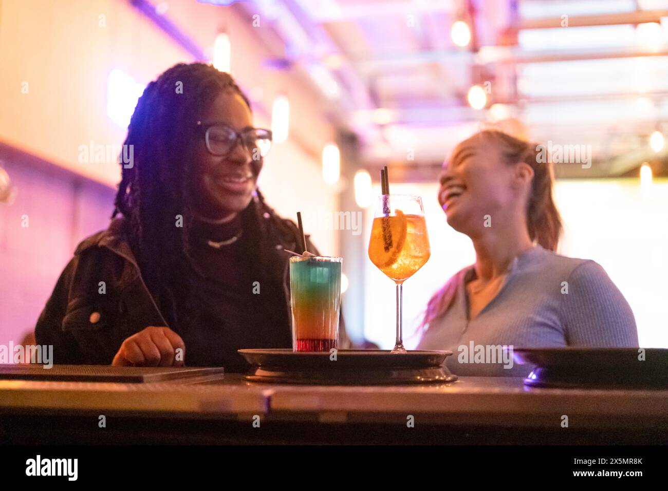 Female friends drinking cocktails at bar counter Stock Photo - Alamy
