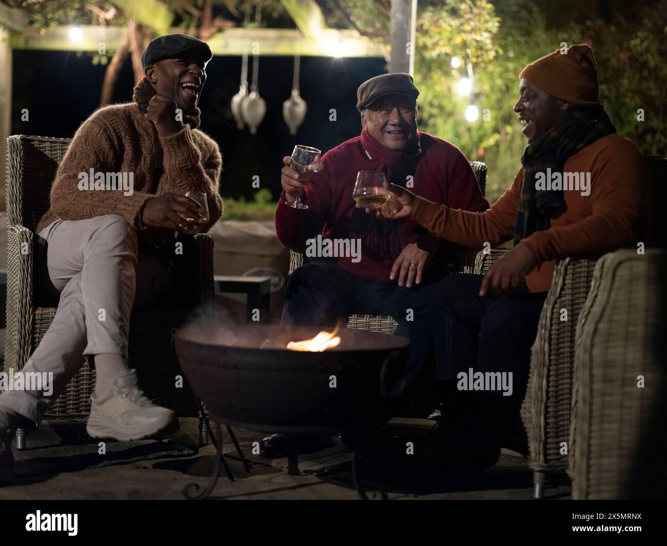 Male friends relaxing by fire pit and raising toast Stock Photo - Alamy