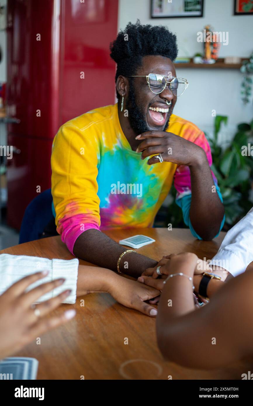 Man laughing while holding hands with friends at table Stock Photo - Alamy